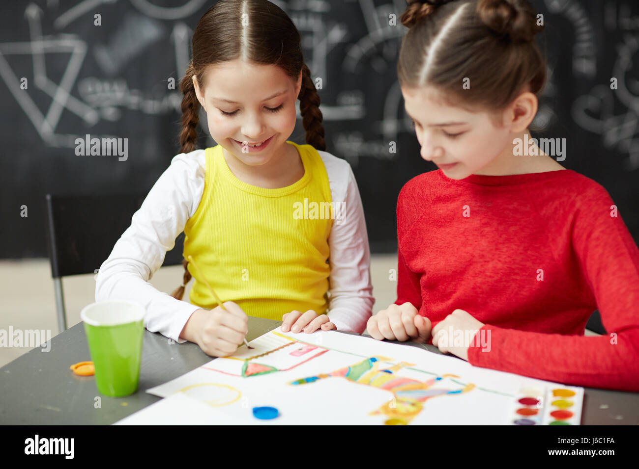 Portrait of two smiling little girls painting pictures together in art ...