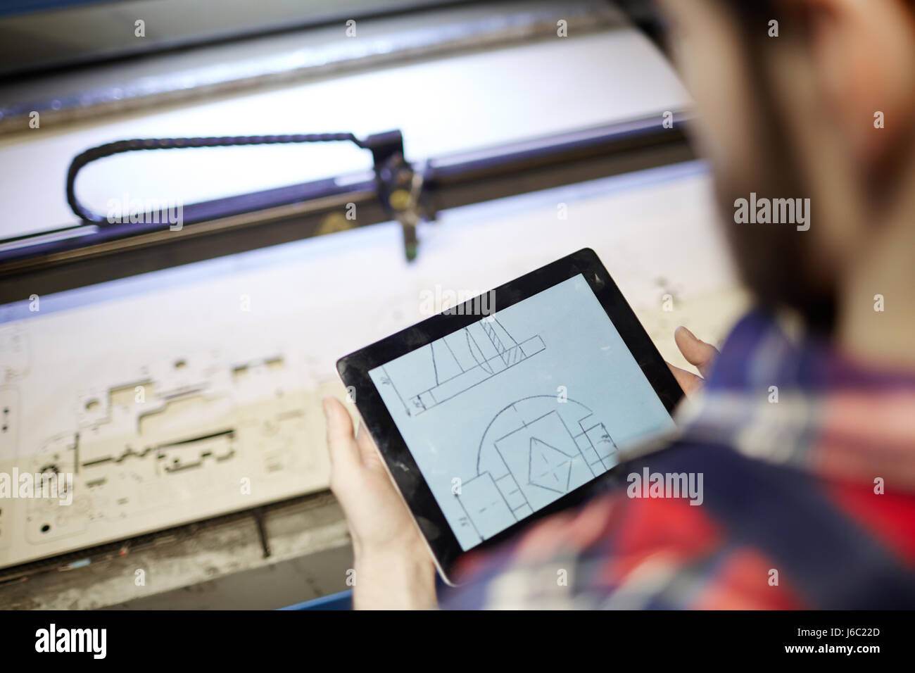 High angle shot of factory worker using digital tablet to operate laser ...
