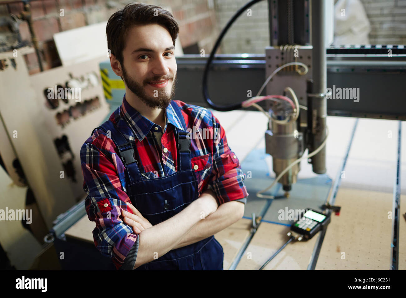 Portrait of handsome factory worker posing in workshop with machines ...