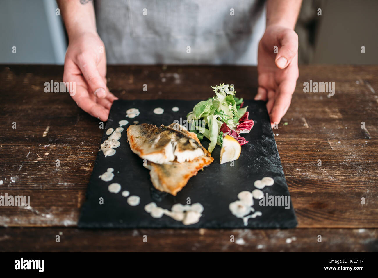 Chef decorate with vegetables dish of fried fish on wooden tray. Fresh ...