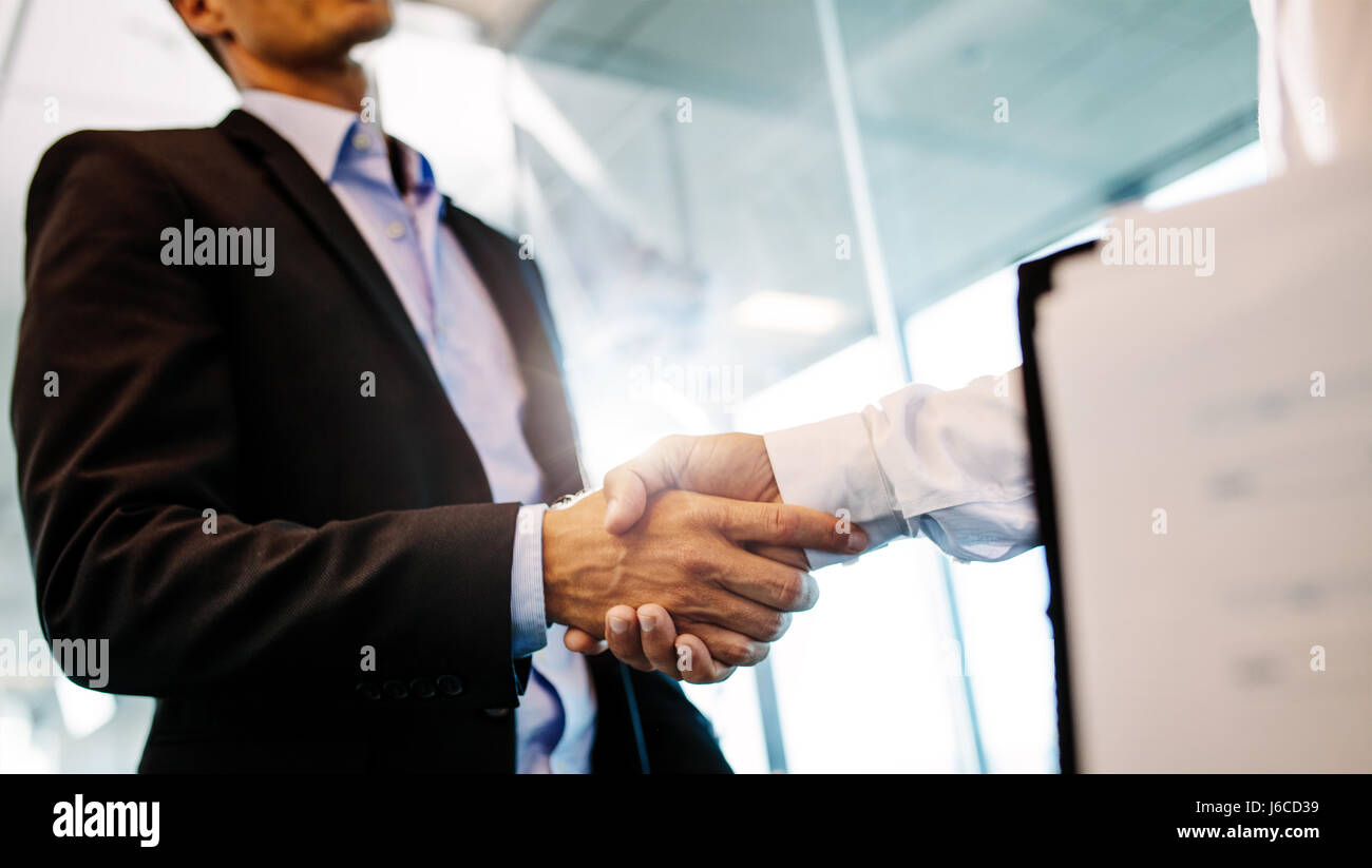 Close-up of two business people shaking hands in office. Cropped shot of handshake after ...