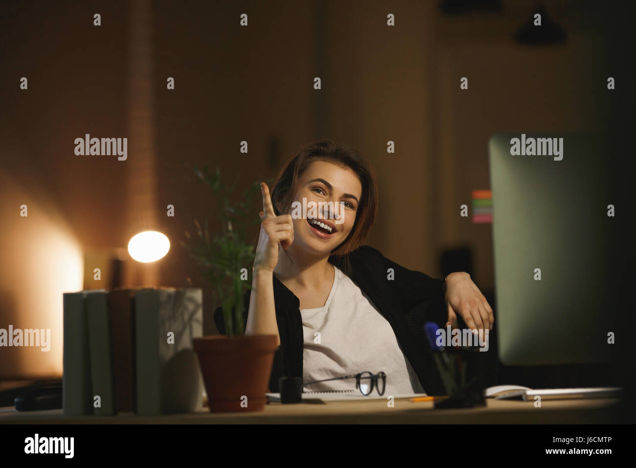 Photo of happy young lady designer sitting in office at night using ...