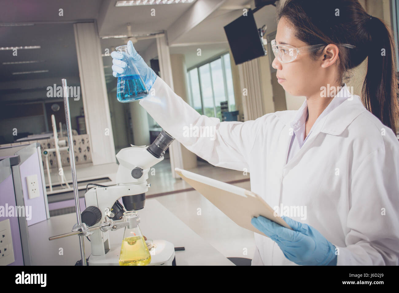 Young scientist with flask of sample substance and tablet computer in ...