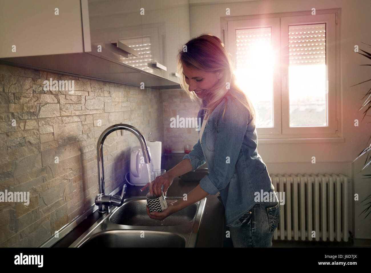 Beautiful smiling young woman washing a cup in kitchen at sunset Stock ...