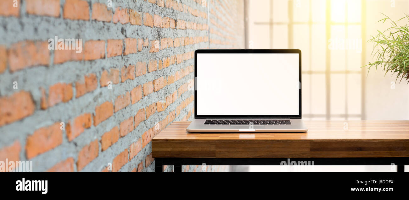 Blank screen laptop on wooden table red brick wall in sunrise ...