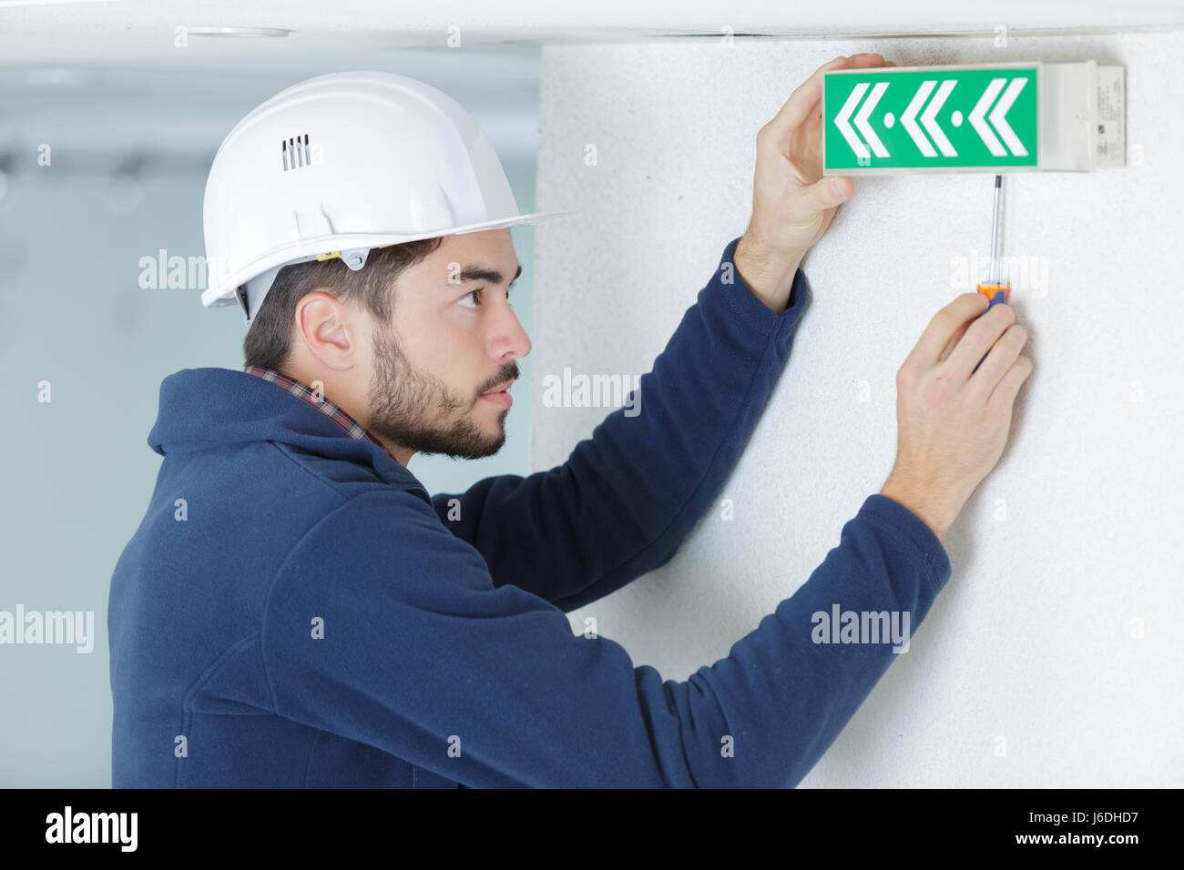 Man fitting illuminated exit sign to wall Stock Photo - Alamy