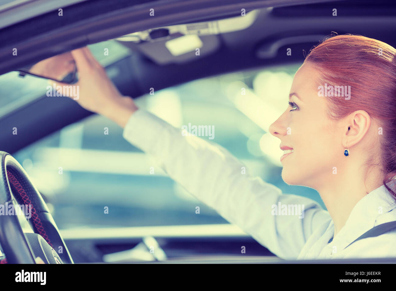 Happy young woman driver looking adjusting rear view car mirror, making ...