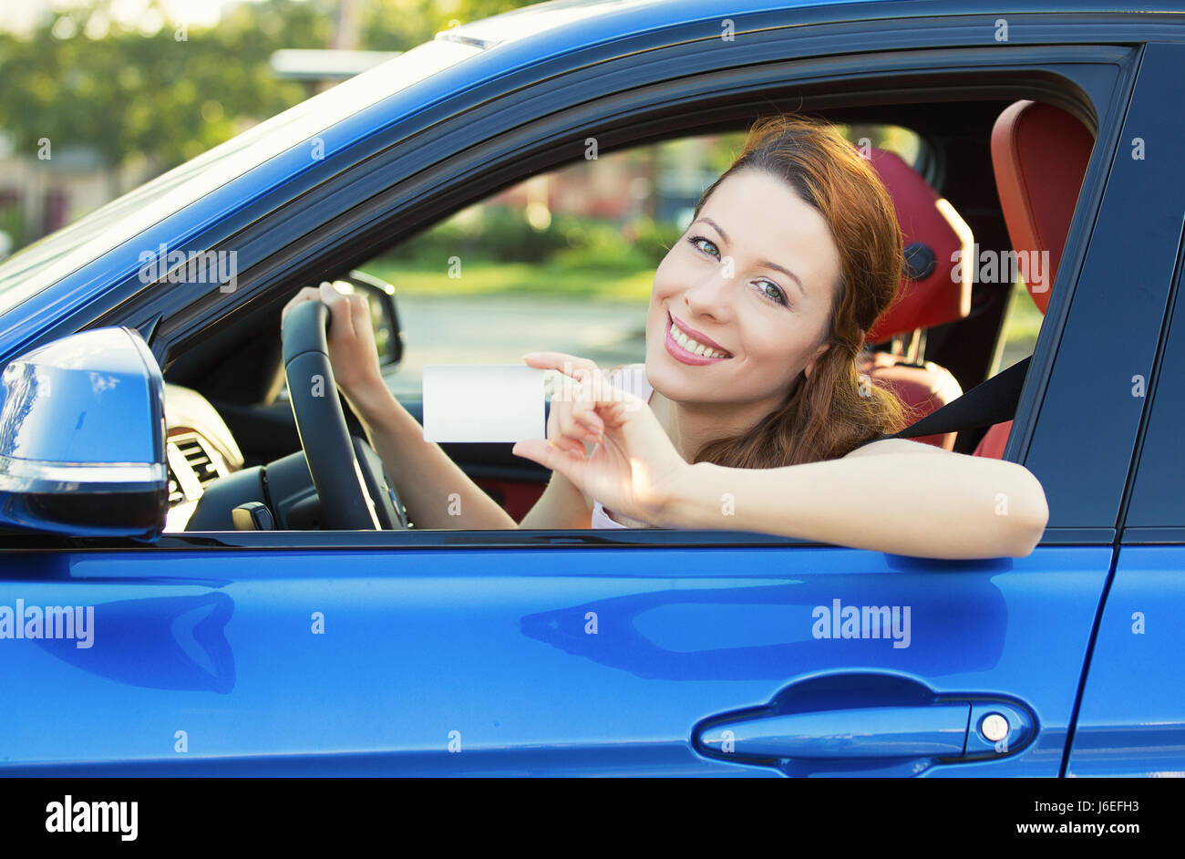 Young woman in new car showing blank drivers license or sign out ...