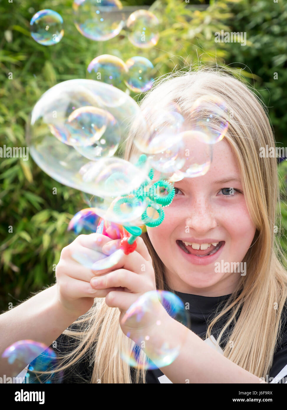 Ten year old blonde girl uses a small machine to blow bubbles at the ...