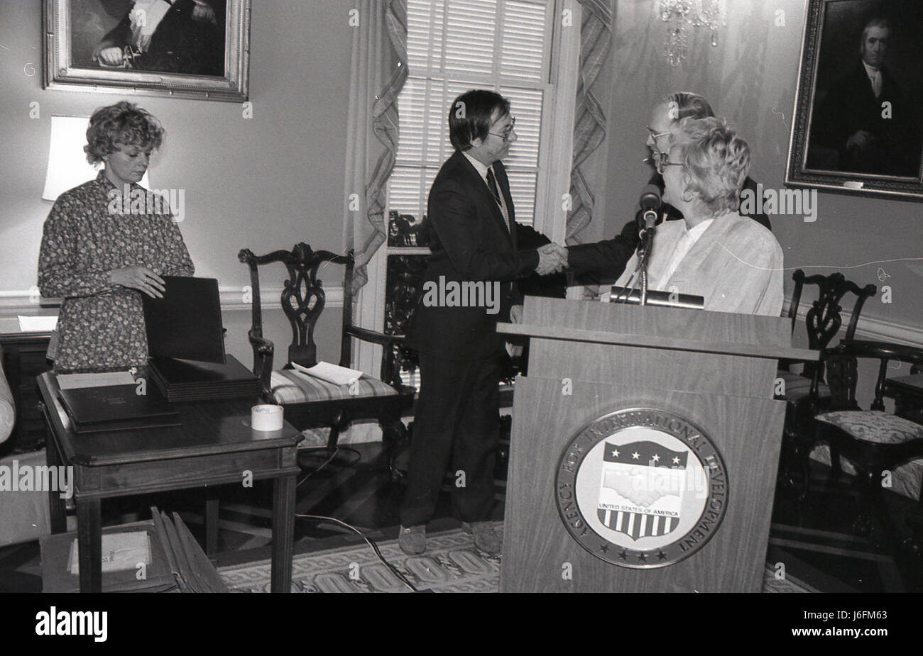 MAN GREETING ANOTHER MAN WITH A WOMEN AT THE PODIUM AND ANOTHER WOMEN ...