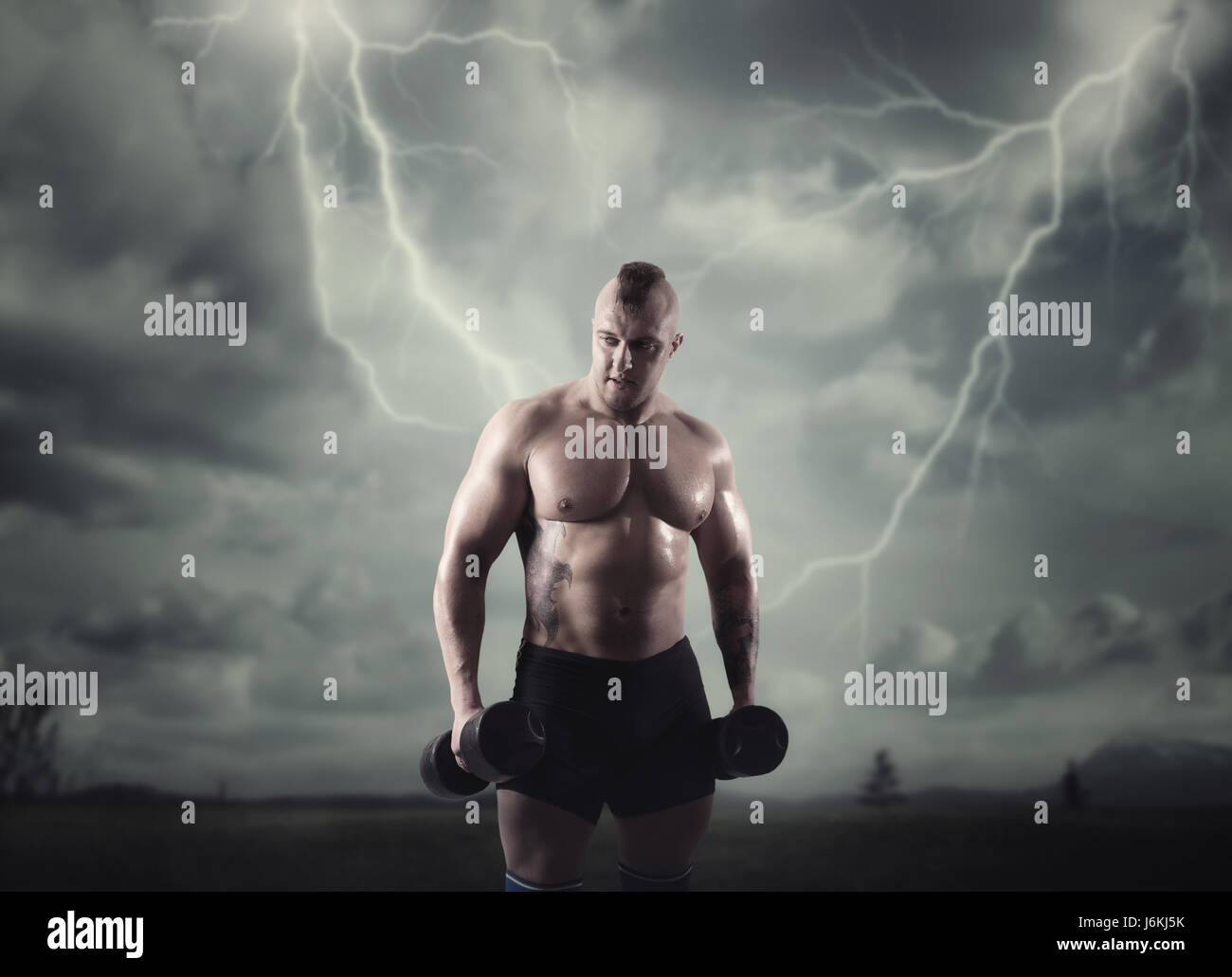 Muscular male athlete with dumbbells, lightning in dark sky on ...