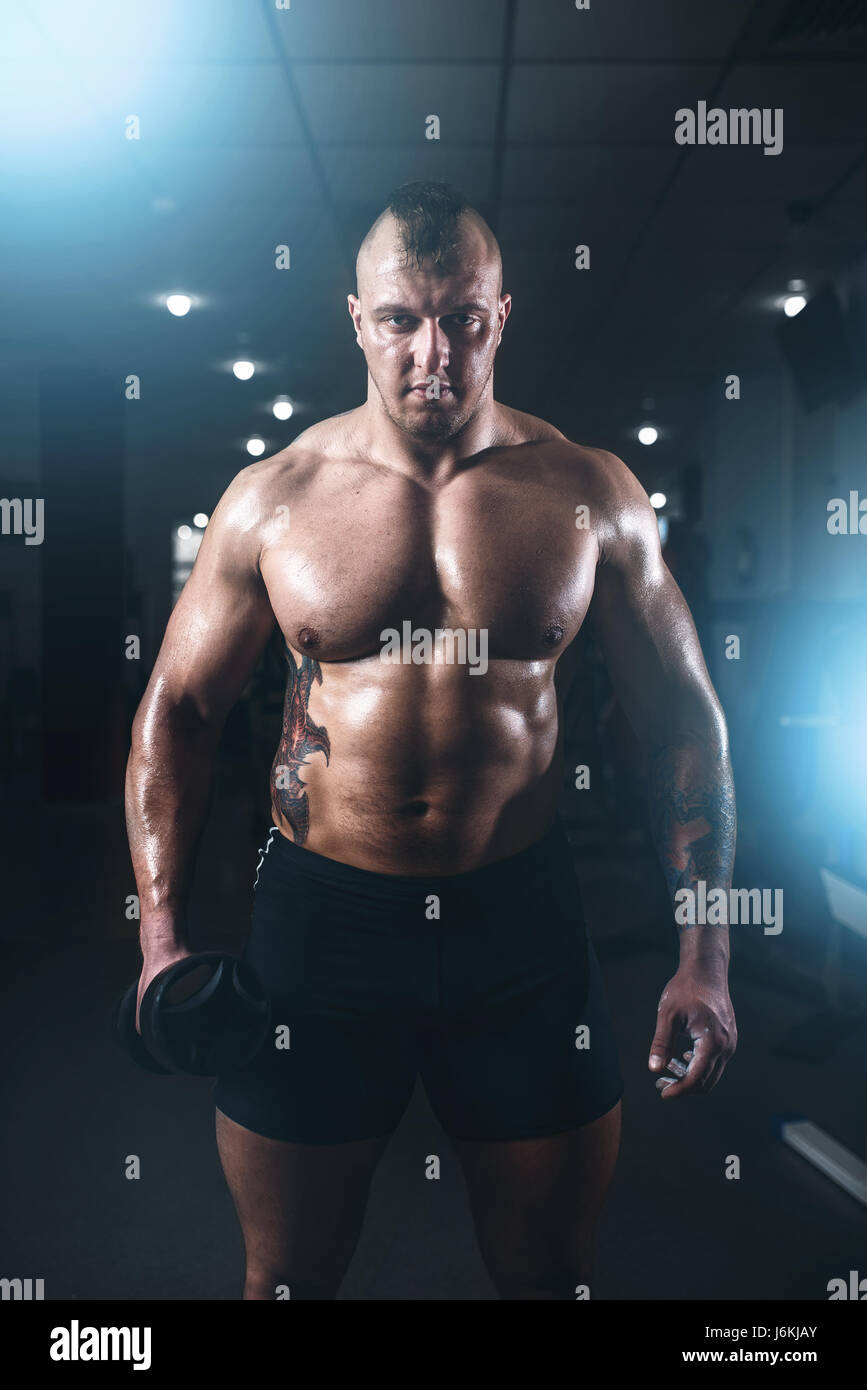 Muscular male athlete posing with dumbbell in sport gym. Fitness ...