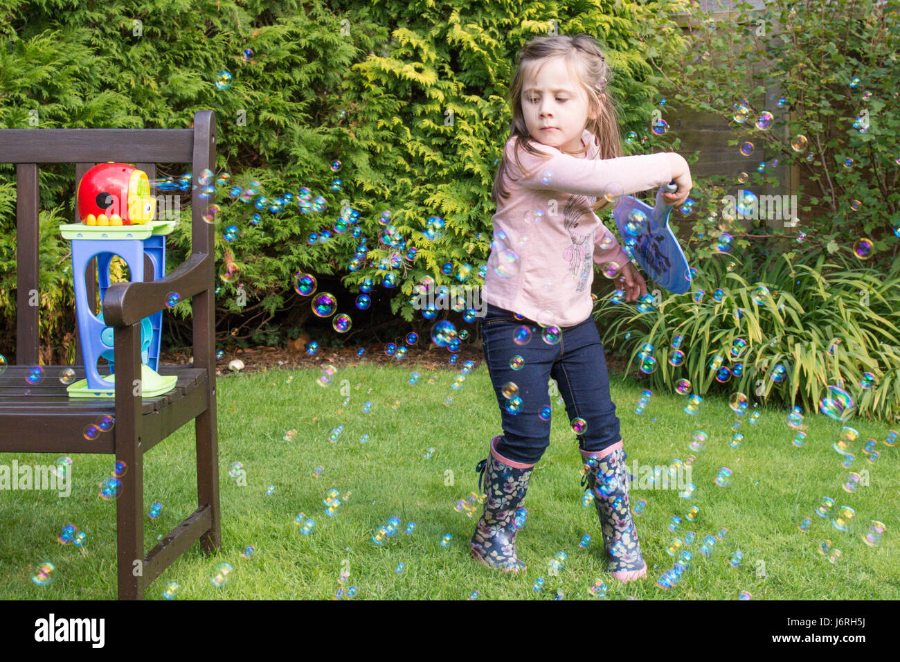 three year old girl hitting with a bat bubbles made by a bubble machine ...