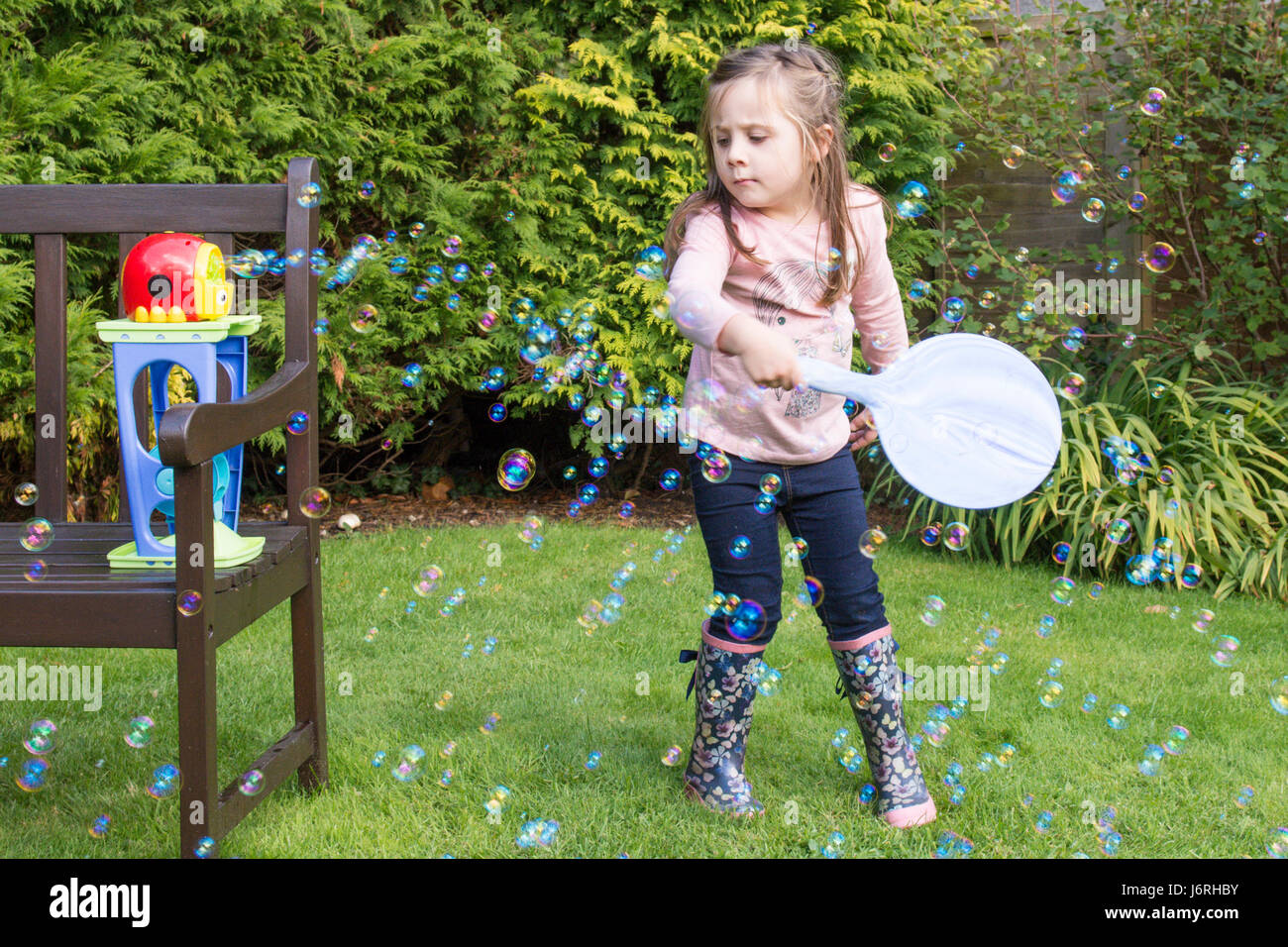 three year old girl hitting with a bat bubbles made by a bubble machine ...
