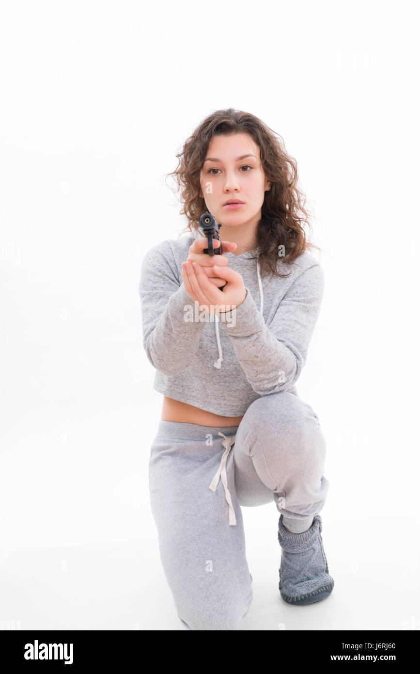 Young girl in a tracksuit with a gun. Beautiful young woman is aiming a ...