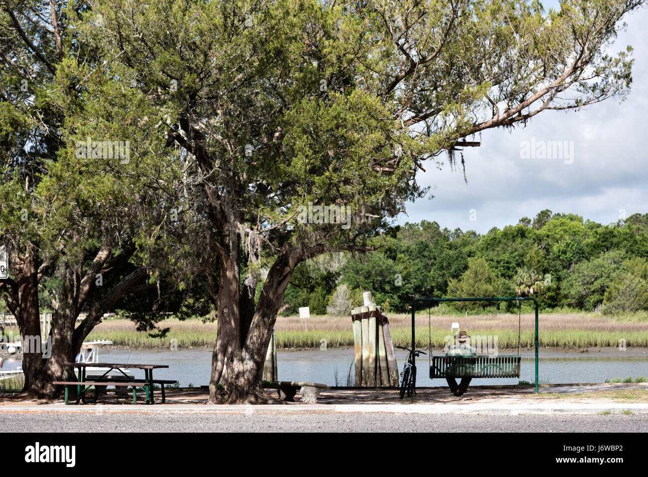 A man sits on a park bench swing along Jeremy Creek in the tiny hamlet ...