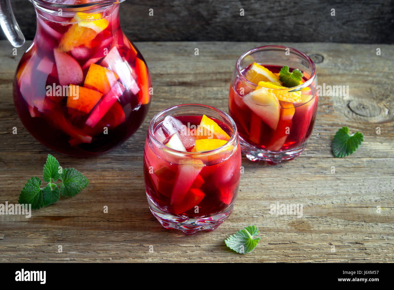 Red wine sangria or punch with fruits and ice in glasses and pincher ...