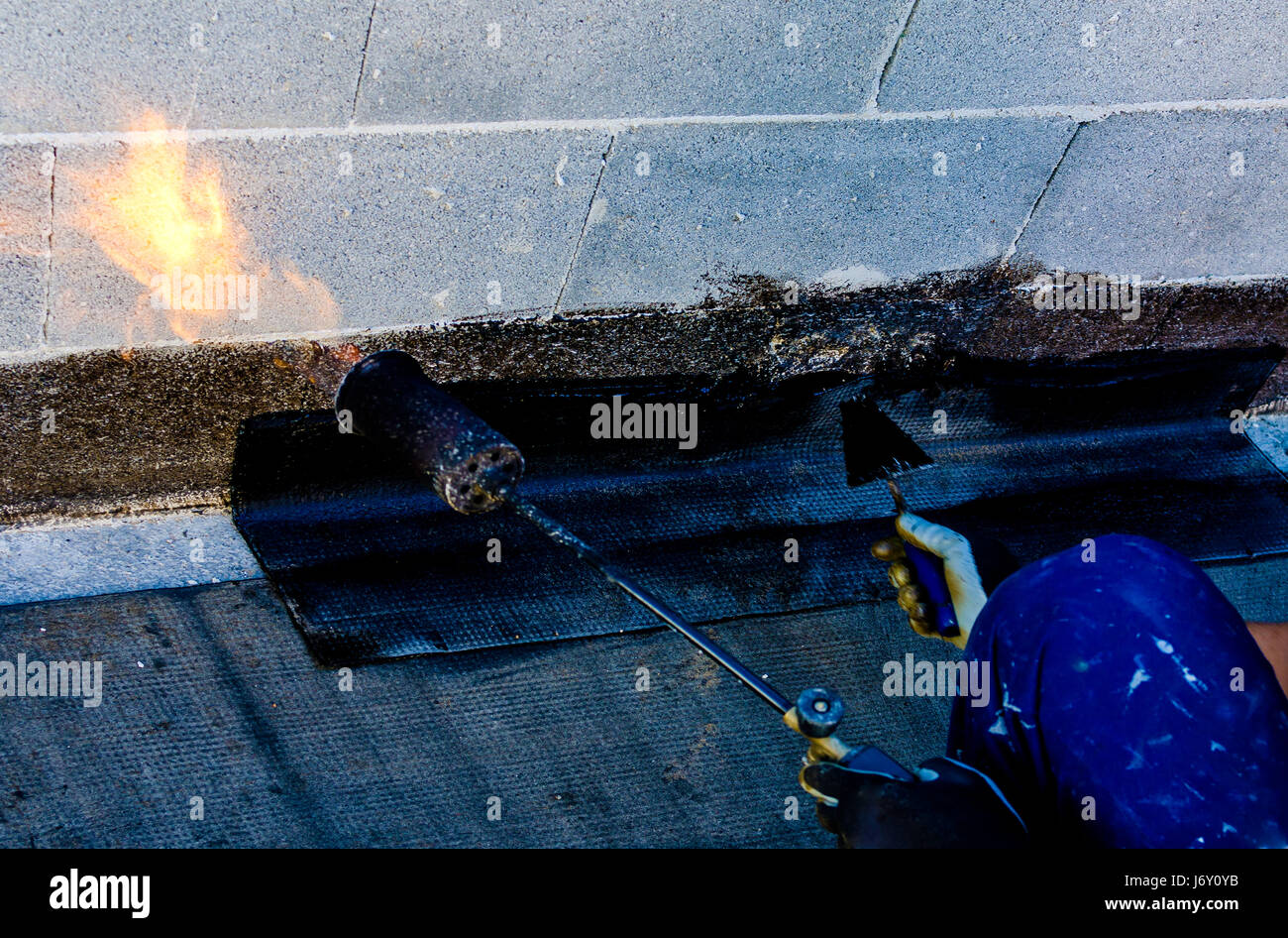 Roofer installing rolls of bituminous waterproofing membrane for the waterproofing of a terrace ...