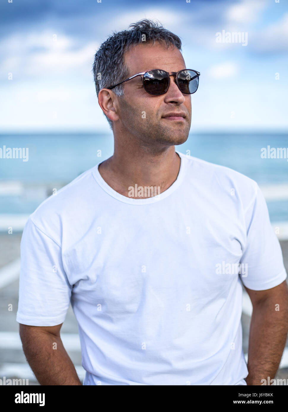 Tanned man in a white T-shirt and sunglasses. In the background - ocean ...
