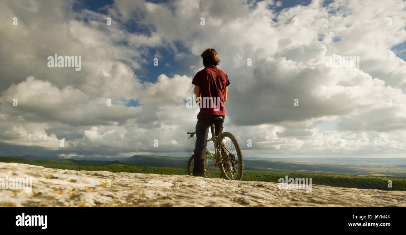 man on bicycle near a cliff with covered by forest hills Stock Photo ...