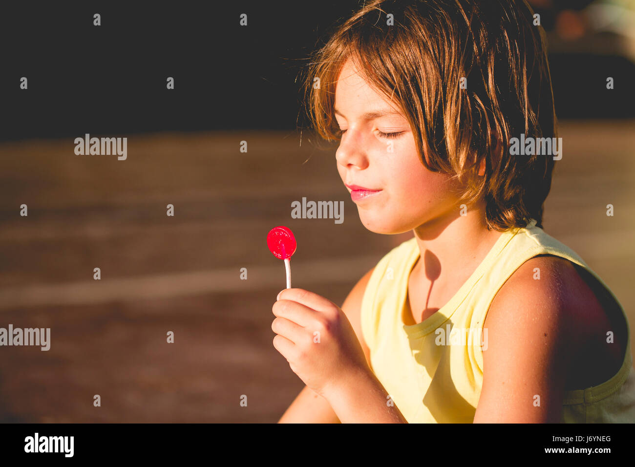Boy sitting in sun eating a lollipop Stock Photo - Alamy