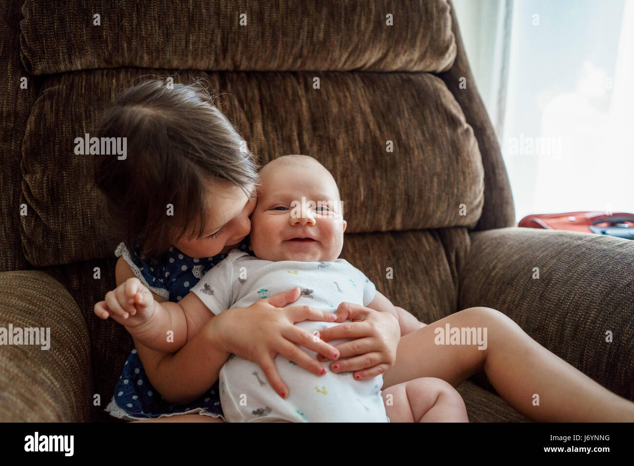 Girl sitting in chair cuddling a baby boy Stock Photo - Alamy