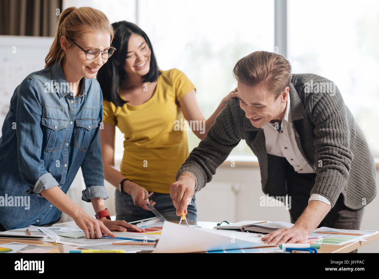 Positive happy designers standing around the table Stock Photo - Alamy