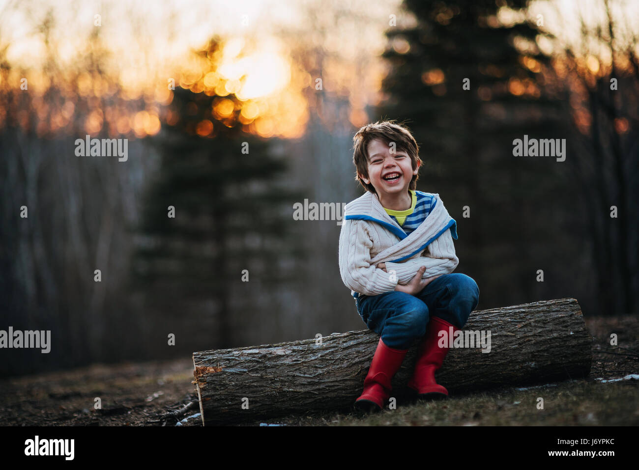 Boy sitting on a log laughing Stock Photo - Alamy