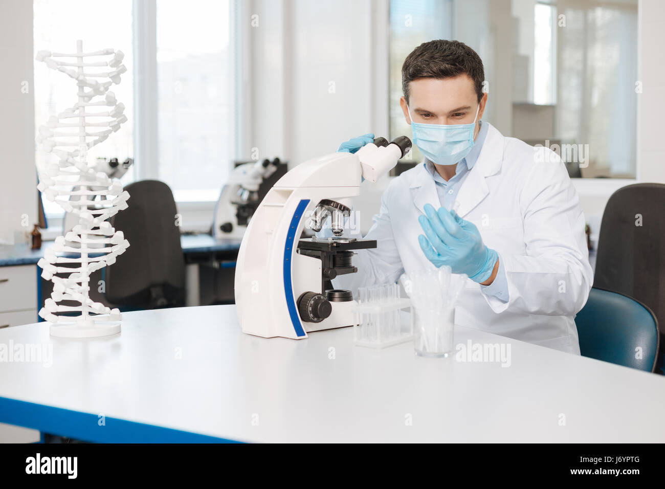 Man scientist in face mask sitting near microscope Stock Photo - Alamy