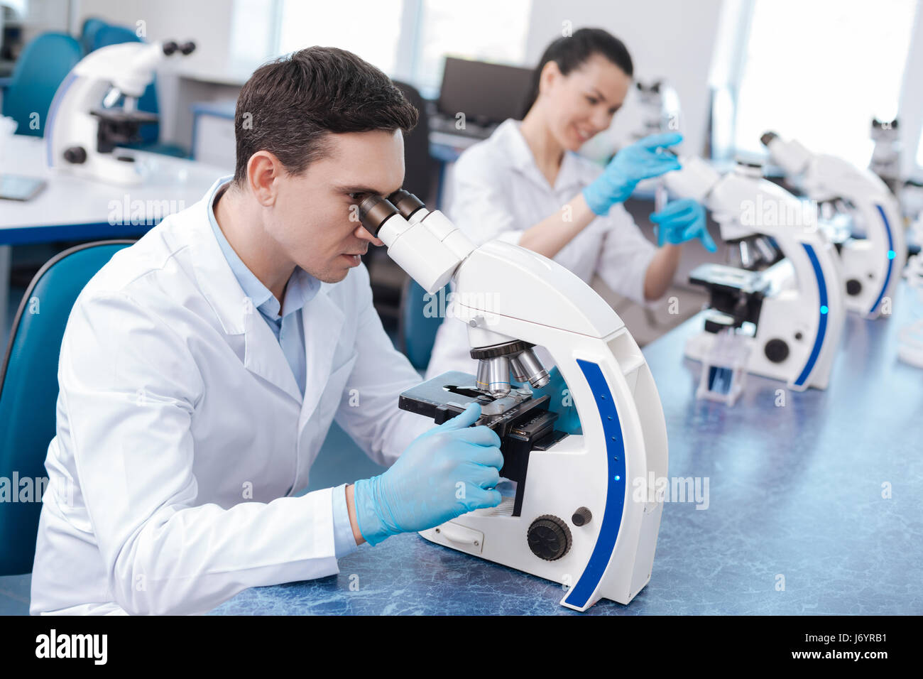Very attentive lab assistant working with microscope Stock Photo - Alamy
