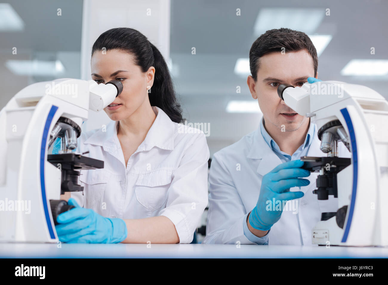 Two competent lab assistants looking into microscope Stock Photo - Alamy