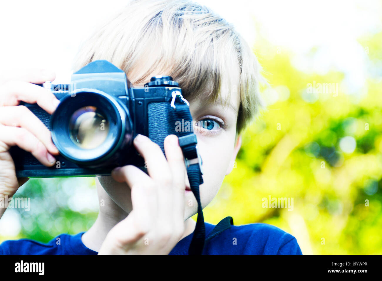 Child blond boy with an old camera shooting outdoor. Kid taking a photo ...