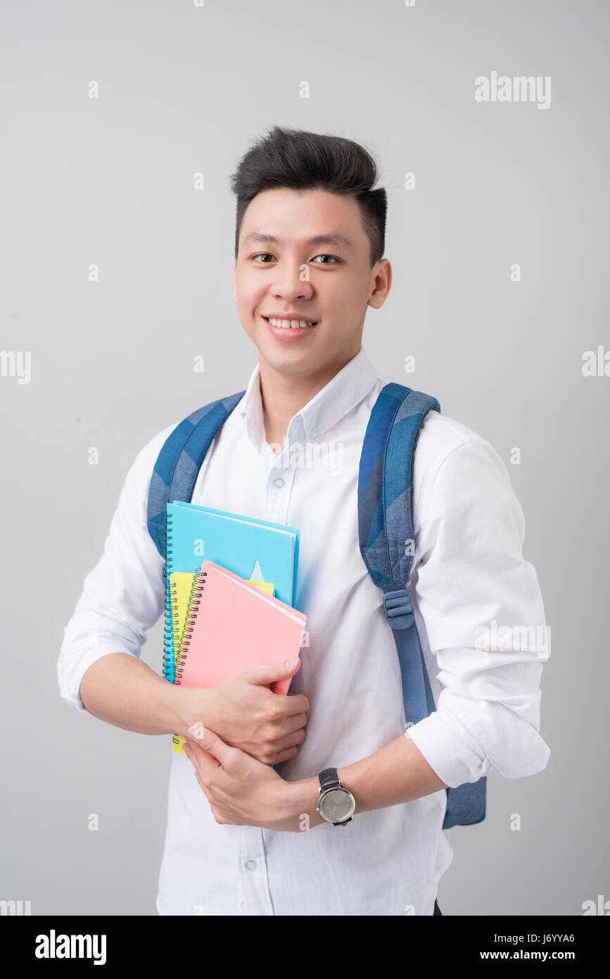 Happy casual asian male student holding books isolated on a gray ...