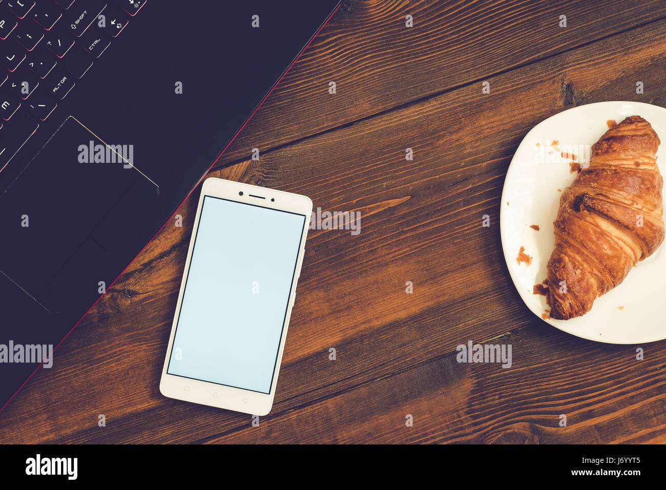 Workspace with laptop, smartphone and croissant on wooden desk Stock ...