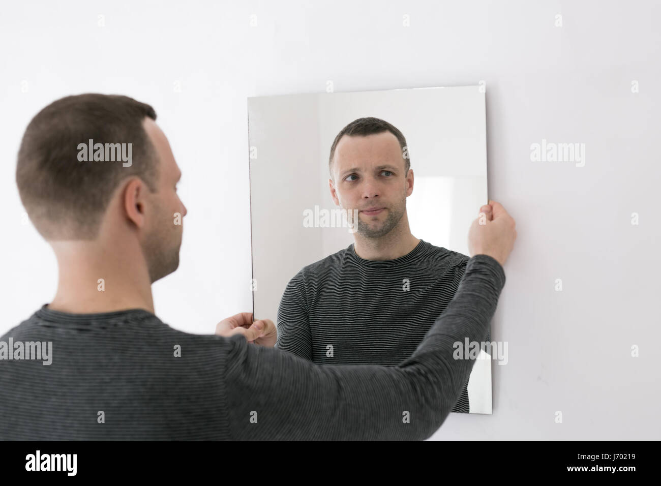 Studio portrait of young man standing near white wall with mirror Stock ...