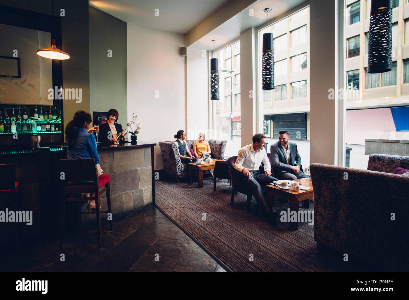 Full room shot of an active hotel bar and cafe. There are people ...