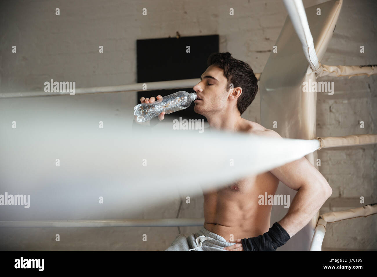 Young sportsman sitting in the boxing ring and drinking water from ...