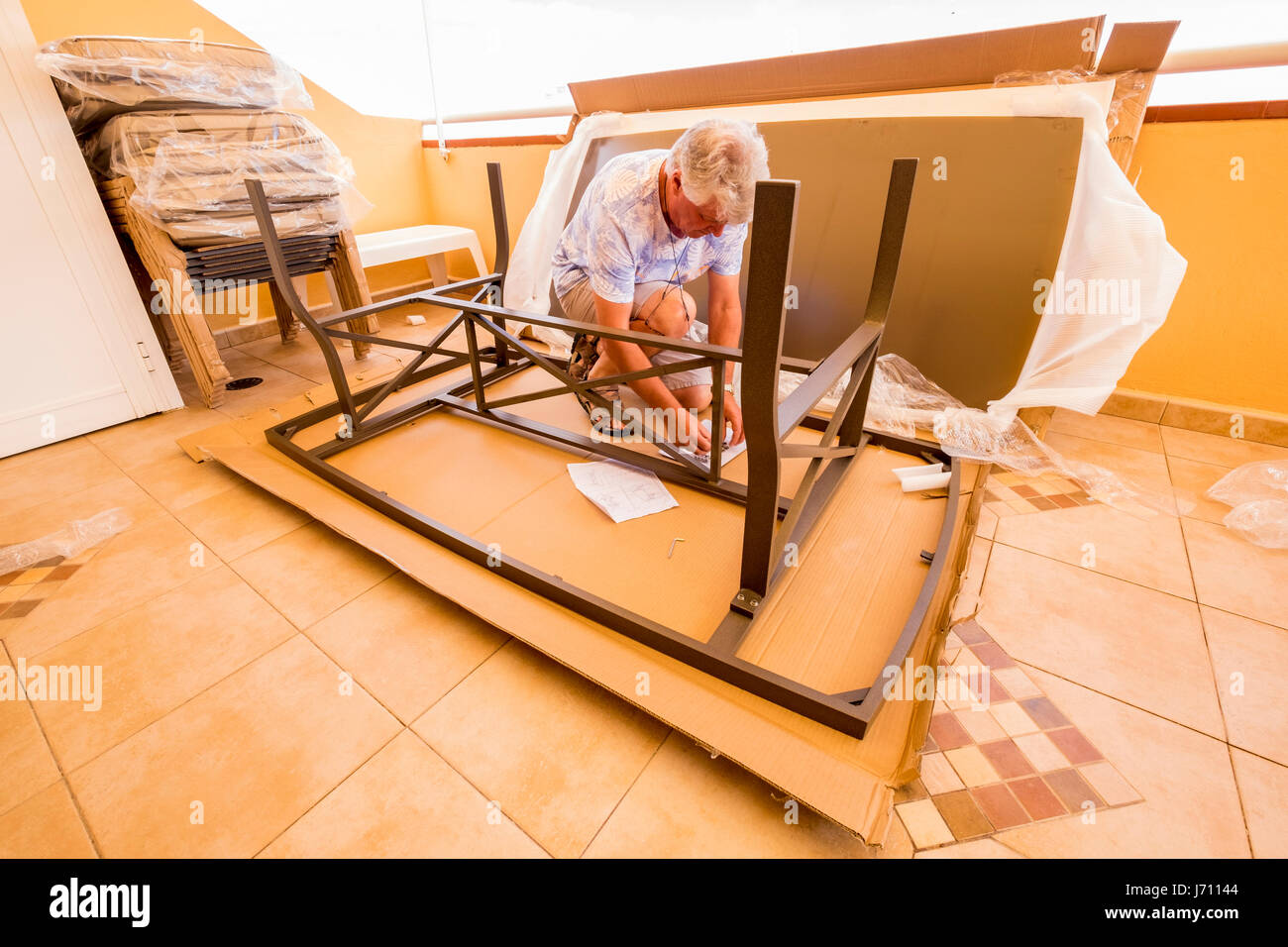 Middle aged man assembling flat packed table on a terrace Stock Photo ...