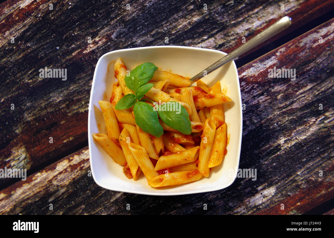 A plate of penne pasta with tomato sauce on wooden table Stock Photo ...