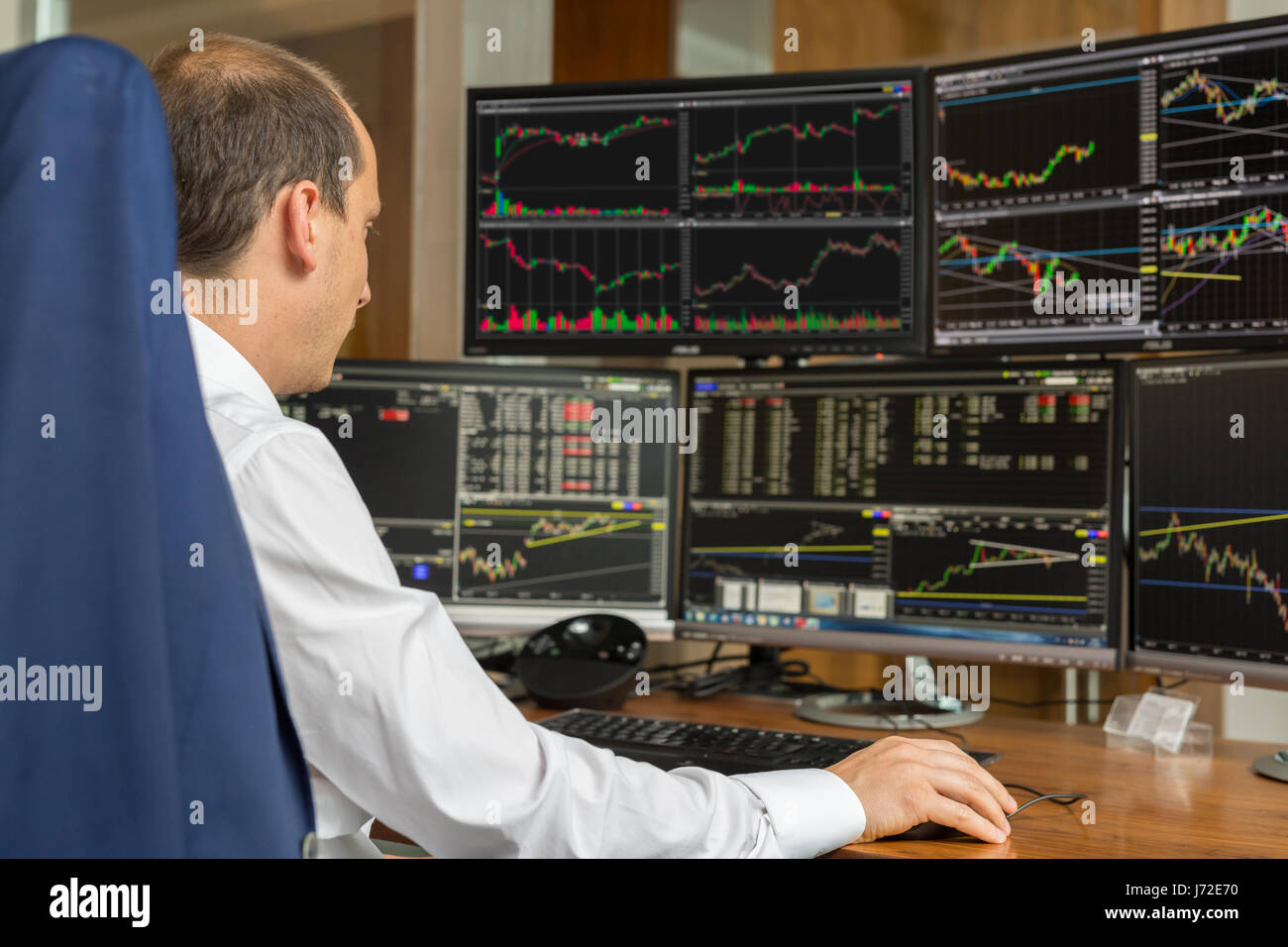 Rear View Of Stock Trader Analyzing Data At Multiple Computer Screens