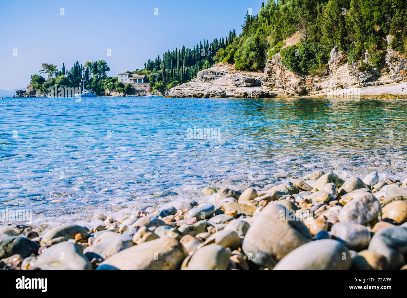 Pebble beach near Kalami with pine and cypress trees and an yacht at ...