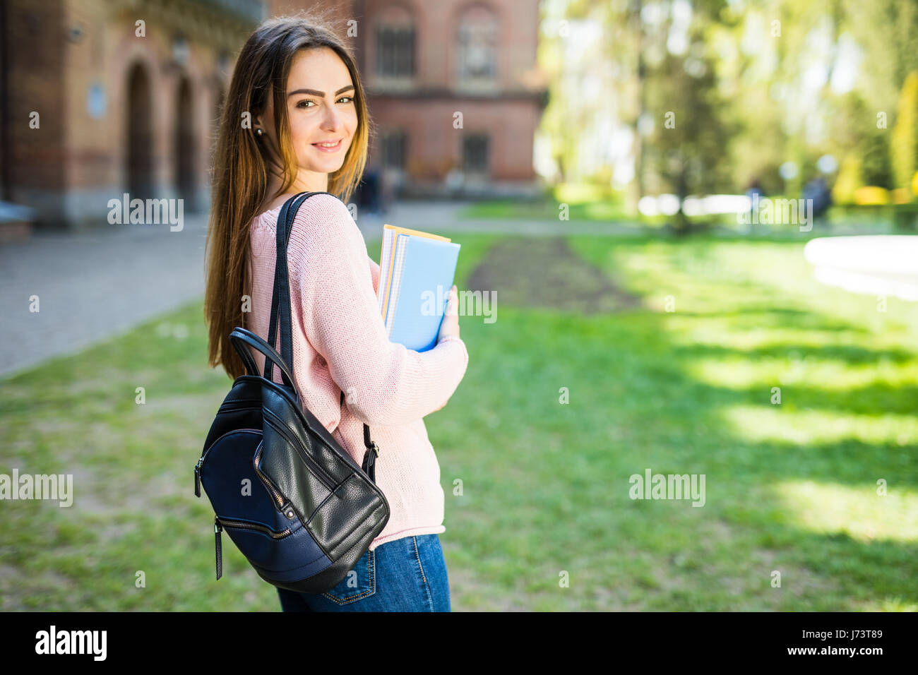 American university student smiling with coffee and book bag on campus ...