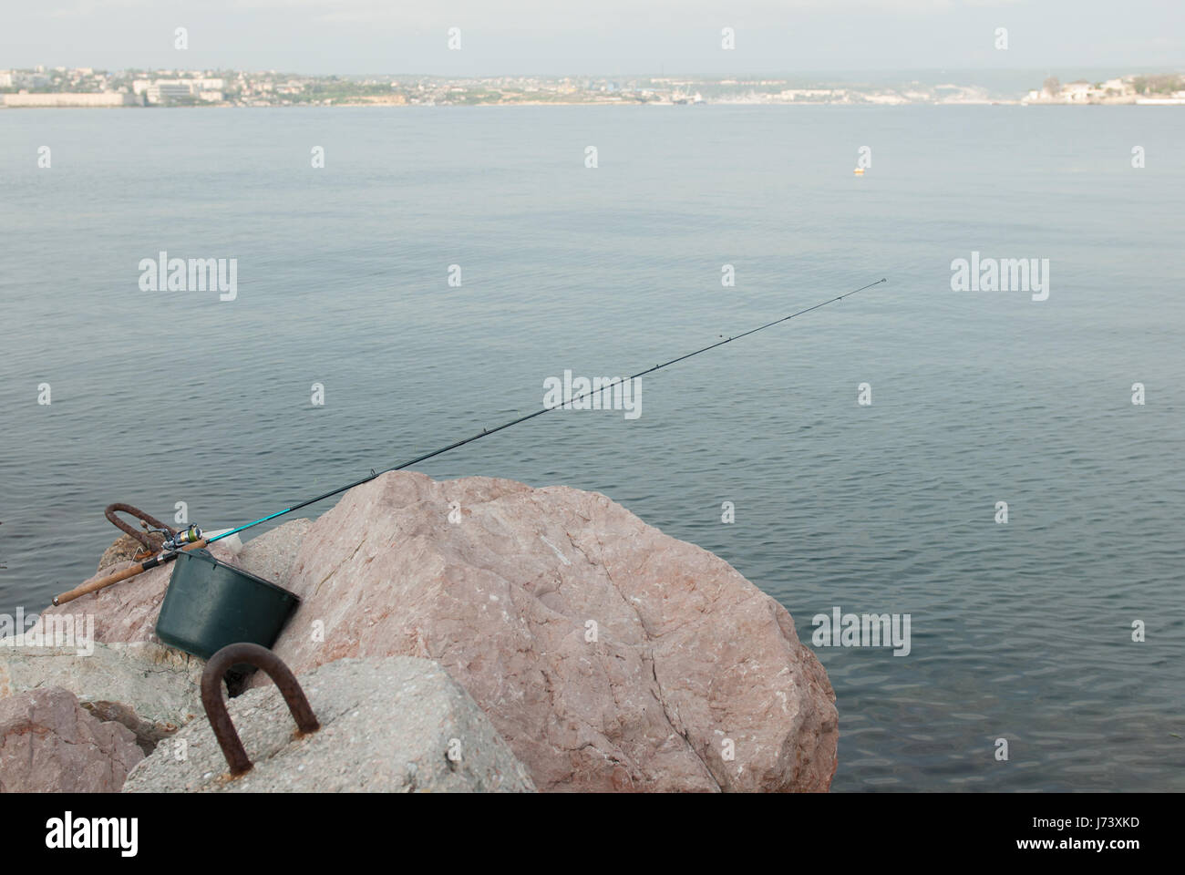 fishing rod and green bucket lying on the stone near breakwater on sea ...