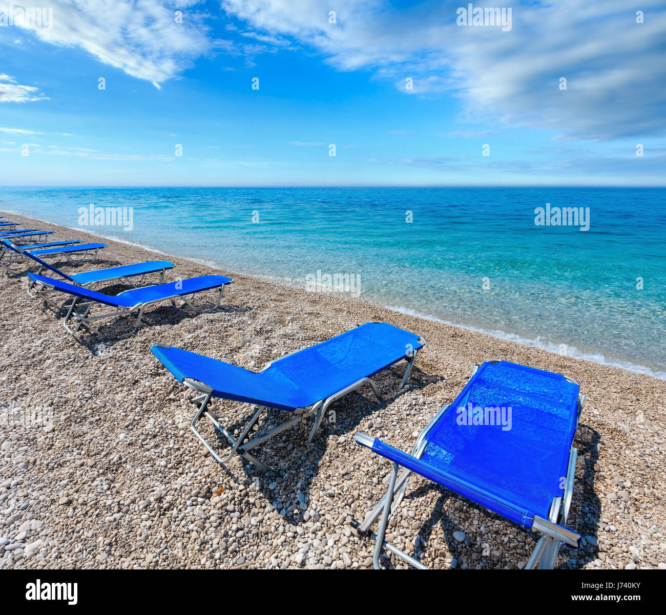 Summer morning beach with sunbeds, gray pebble and blue cloudy sky ...