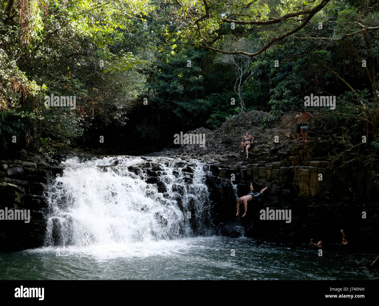 Tourists jump into a deep pool at the twin falls waterfall on the road ...