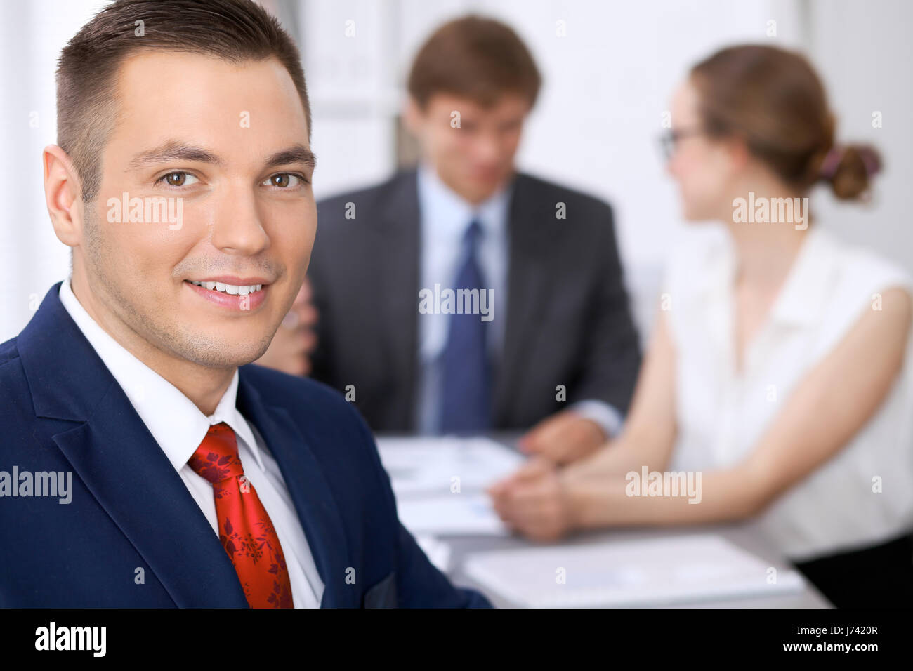 Portrait of cheerful smiling business man against a group of business ...