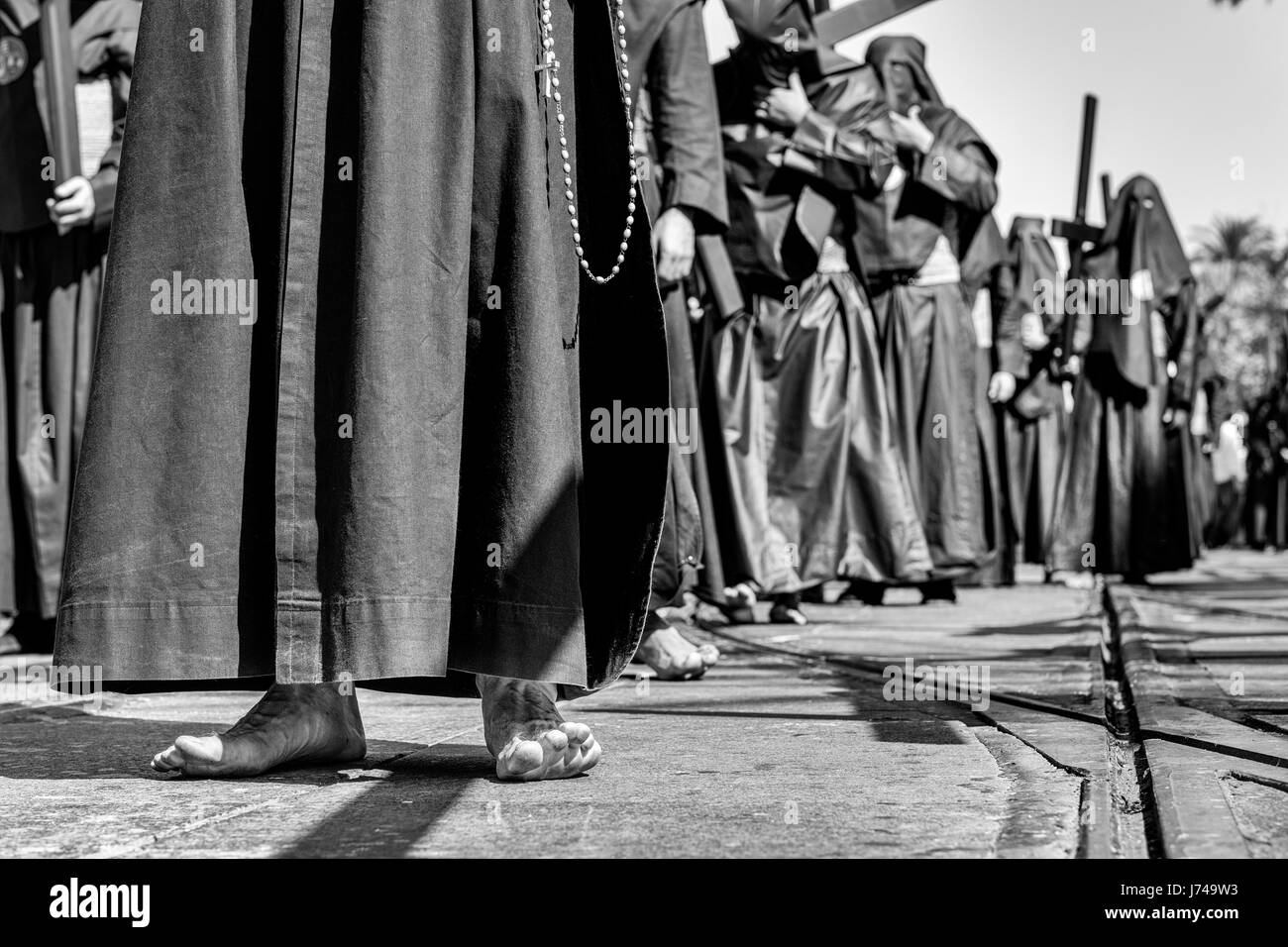 Penitents march barefoot along with the procession carrying a cross in ...