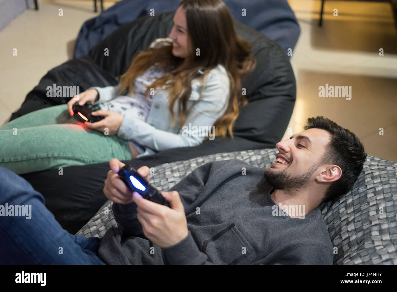 happy couple friends playing video games with joystick sitting on Bean ...