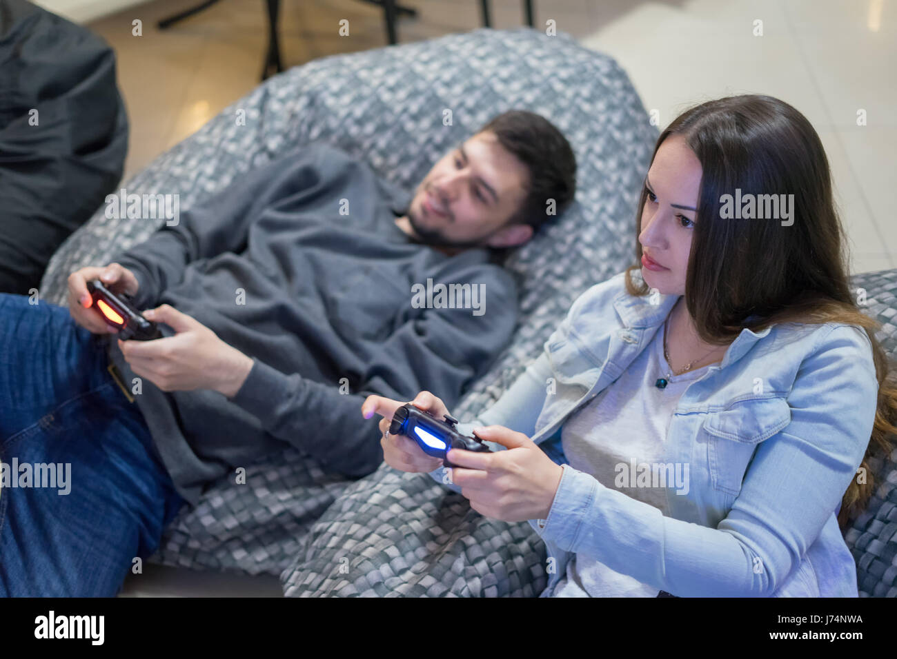 happy couple friends playing video games with joystick sitting on Bean ...