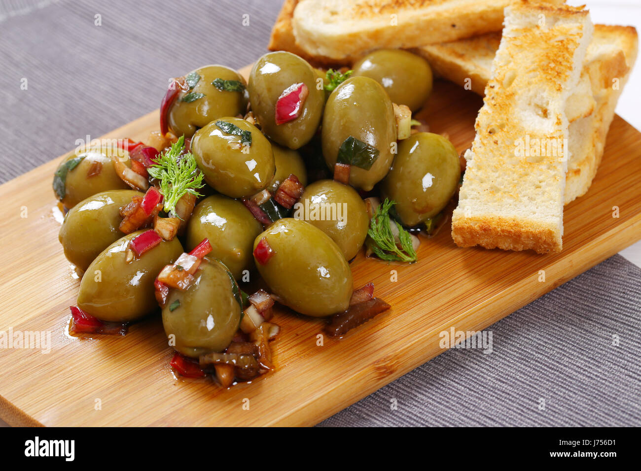 pile of marinated green olives with toasts on wooden cutting board ...